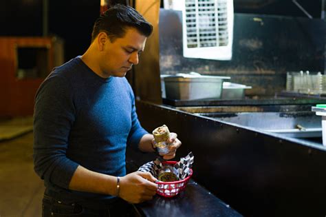 부리또를 움켜쥐고 형형색색의 푸드 트럭 근처에서 바구니를 들고 어두운 별이 빛나는 하늘 아래에서 늦은 밤 멕시코 길거리 요리를 즐기는 남자 건강에 좋지 않은 음식에 대한