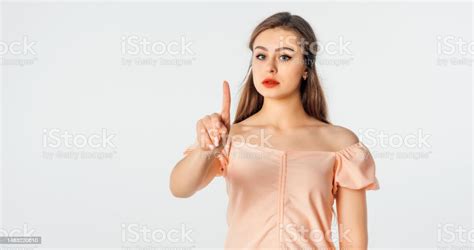 젊은 여자는 눈살을 찌푸리고 매우 불만족스러워 보이고 집게 손가락을 흔들어 아무 말도하지 말고 누군가를 꾸짖거나 말하고 허락하지 않고 흰색 배경 위에 서 있습니다 손가락에
