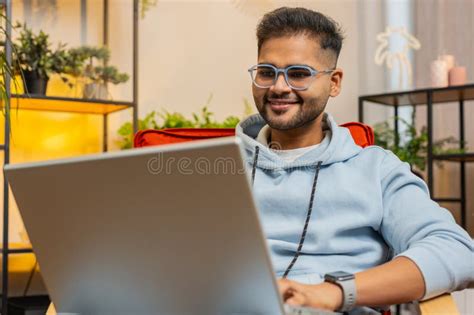 Young Man Freelancer Sitting On Chair Working On Laptop Pc Browsing Internet In Living Room At