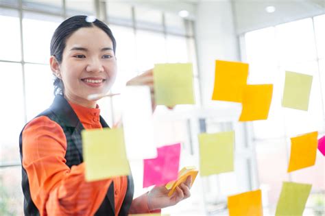 사무실에서 프로젝트에 종사하는 행복한 미소 아시아 비즈니스 여성은 아이디어를 공유하기 위해 포스트 페이퍼와 필기 노트를 사용하고 유리 벽에 붙어 아이디어 성공적인 창의력