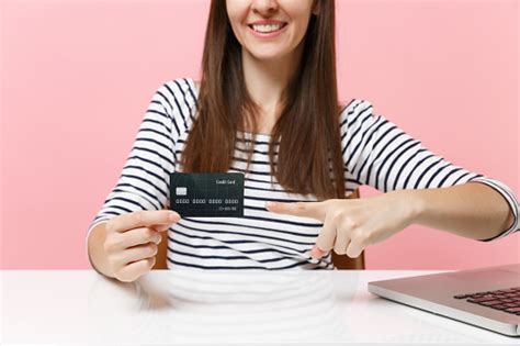 신용 카드에 검지 손가락을 가리키는 캐주얼 옷에 여자의 이미지를 자른 파스텔 핑크 배경에 고립 된 흰색 책상에 앉아 성과 비즈니스 경력 개념입니다 광고에 대 한 공간을 복사