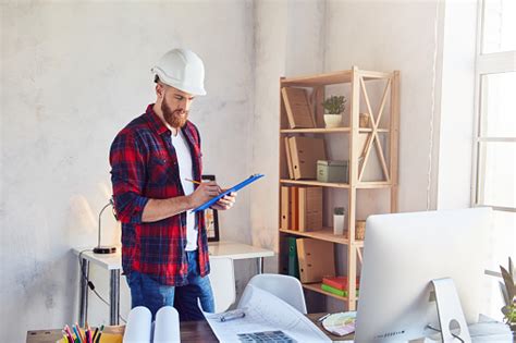 사무실에 서서 도면을 작업하는 단단한 모자를 쓴 디자이너 개념에 대한 스톡 사진 및 기타 이미지 개념 개발 건축가