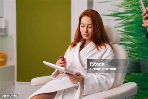 흰 목욕 가운을 입은 아름다운 여성 환자는 현대 건강 미용 센터에서 성형 수술을 하기 전에 계약서에 서명합니다 미용 스파 뷰티 트리트먼트의 개념 30 34세에 대한 스톡