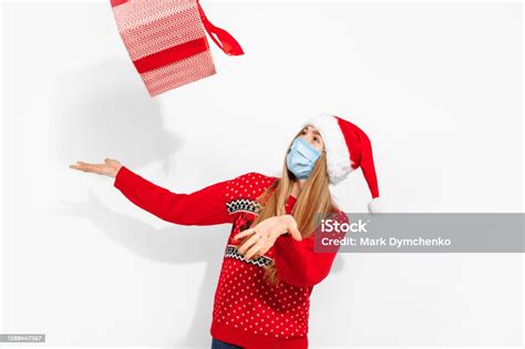 산타 클로스 모자와 그녀의 얼굴에 의료 마스크를 흥분 소녀는 기뻐하고 흰색 배경에 크리스마스 선물 상자를 던져 12월에 대한 스톡 사진 및 기타 이미지 Istock