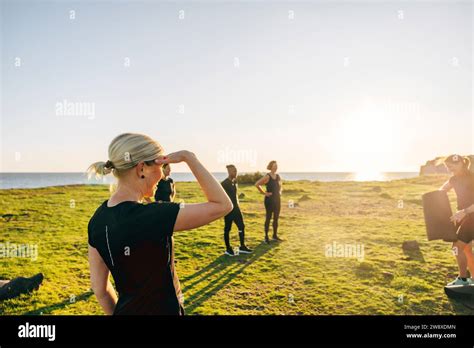 Woman Shielding Eyes During Group Training On Sunny Day At Beach Stock