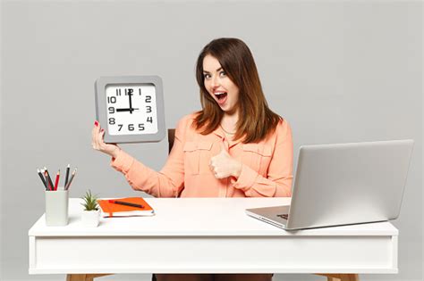 파스텔 옷에 젊은 쾌활 한 여자 회색 배경에 고립 된 Pc 노트북과 책상에서 광장 시계 작업을 들고 엄지손가락을 보여주는 성취 비즈니스 커리어 라이프 스타일 컨셉 복사