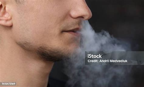전자 담배를 피우는 남자의 클로즈업 남자는 자연스러운 배경에서 전자 담배를 피운다 힙스터는 전자 담배를 피우고 연기의 흐름을 내뿜고 옥외 복사 공간을 낭비합니다 남자에 대한