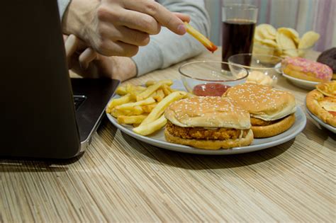 남자는 컴퓨터에서 작동 하 고 패스트 푸드를 먹는다 건강에 해로운 음식 햄버거 소스 감자 도넛 칩 감자 요리에 대한 스톡 사진 및 기타 이미지 Istock