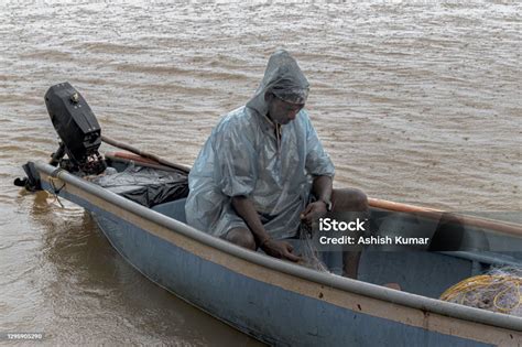 중년 어부는 비옷을 입고 몬순의 장마철에 성공적으로 잡은 후 작은 동력 카누로 어망을 검사합니다 강은 눈에 보이는 비가 내리는 진흙 투성이입니다 사고와 재해에 대한 스톡