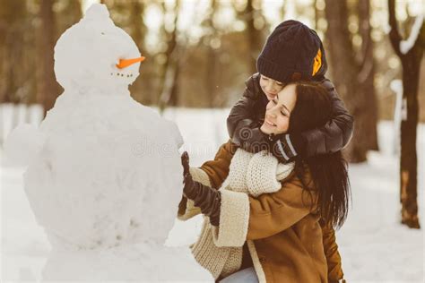 Счастливая семья в теплой одежде Усмехаясь мать и сын делая снеговик внешний Концепция