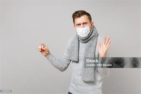 스웨터 스카프 무 균 얼굴 마스크 홀드 온도계 회색 배경에 고립 손을 확산 충격 젊은 남자 건강 한 라이프 스타일 아픈 질병