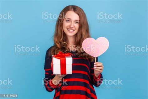 선물 상자를 들고 서서 막대기에 분홍색 하트를 보여주며 사랑으로 카메라를 바라 보는 여성 20 24세에 대한 스톡 사진 및 기타 이미지 20 24세 가지 식물 부위