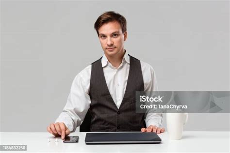 흰색 티셔츠와 회색 조끼를 입은 예쁜 사무직 근로자가 작업 장에서 물건을 정리합니다 노트북 스마트폰 커피 한 잔이 흰색 테이블에 있습니다 T 셔츠에 대한 스톡 사진 및 기타