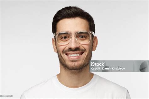 잘생긴 백인 젊은이 얼굴 머리 백색 T셔츠와 투명 한 플라스틱 안경 카메라를 바라보 고 긍정적으로 웃 옷을 입고 회색 배경에 고립의 가로 근접 촬영 Stem 주제에 대한