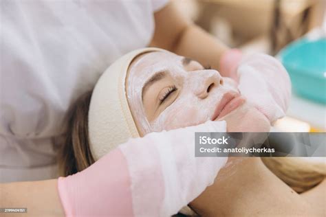 미용실에서 침대에 누워 있는 젊은 여성의 얼굴에 흰색 안면 마스크를 바르는 장갑을 낀 미용사 피부 관리에 대한 스톡 사진 및 기타 이미지 Istock