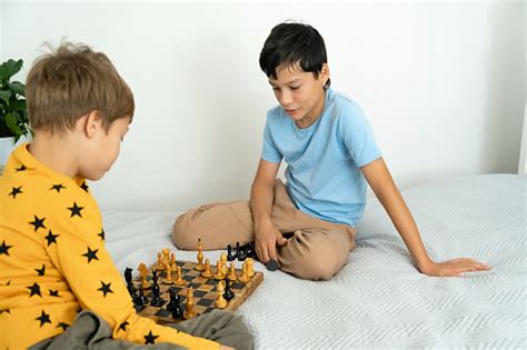 두 명의 백인 소년이 침대에서 집에서 체스를하고 있습니다 형은 어린 아이에게 체스를 가르치고있다 레저 게임 12 13세에 대한