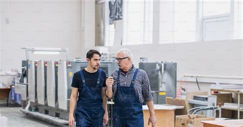 파란색 작업복을 입은 고위 및 젊은 인쇄소 노동자들이 현대 작업장을 건너 작업에 대해 논의합니다 사진 Unsplash의 거래 이미지