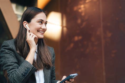 헤드폰을 끼고 웃고 있는 매력적인 비즈니스 여성이 사무실 건물 앞에 서 있다 원격 근무 비즈니스 프리랜서 온라인 쇼핑 E 러닝 도시 개념 공간을 복사합니다 야외에 대한 스톡