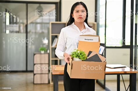 슬프고 화가 난 아시아 여성 회사원이 그녀의 물건이 담긴 골판지 상자를 들고 사무실에 서 있다 20 24세에 대한 스톡 사진 및