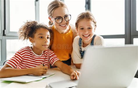 Teacher And Pupils Using Laptop In Sunlit Classroom In School Stock