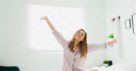 잠옷을 입고 잠에서 깨어나 팔을 뻗은 후 침대에 앉아 있는 매력적인 긍정적인 여성 행복하고 잘 쉬었다고 느끼는 히스패닉 여성 사진 Unsplash의 리넨 이미지