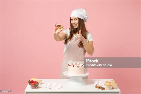 요리사 요리 과자 또는 베이커 앞치마 화이트 T 셔츠 모자 요리사 모자 요리 케이크 또는 테이블에 컵 케이크를 잡아 스튜디오에서 분홍색 파스텔 배경에 고립 비트 코인 동전