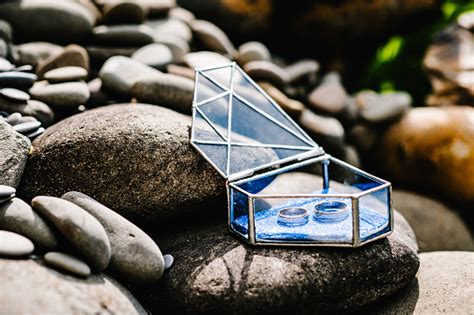 웨딩 골드 실버 약혼 반지는 다이아몬드 모양의 유리 모양의 금속 상자에 거짓말 둥근 큰 돌의 배경에 화려한 파란색 표면에 결혼 반지 닫 다 결혼 의식에 대한 스톡 사진 및