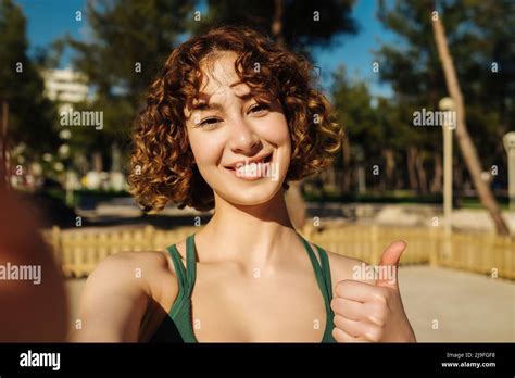 Image Of Happy Young Redhead Woman Wearing Green Sports Bra Standing On City Park Outdoors