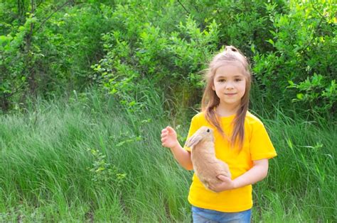 Premium Photo Little Cute Girl Plays With A Real Ginger Rabbit On A Background Of Green Plants