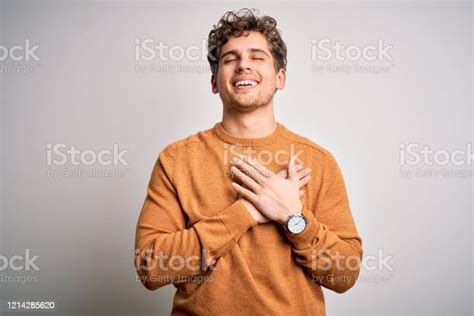 젊은 금발 잘생긴 남자 곱슬 머리 흰색 배경에 캐주얼 스웨터를 입고 얼굴에 닫힌 눈과 감사 제스처가슴에 손으로 미소 건강 개념 남자에 대한 스톡 사진 및 기타 이미지