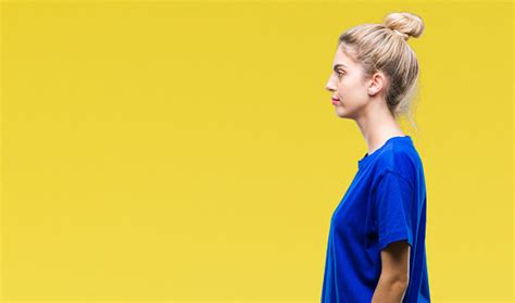 젊은 아름 다운 금발 및 파란 눈 여자는 고립 된 배경 위에 파란 T셔츠를 입고 측면을 찾고 자신감 있는 미소로 자연 스러운 얼굴로 프로필 포즈를 취하십시오 옆모습에 대한