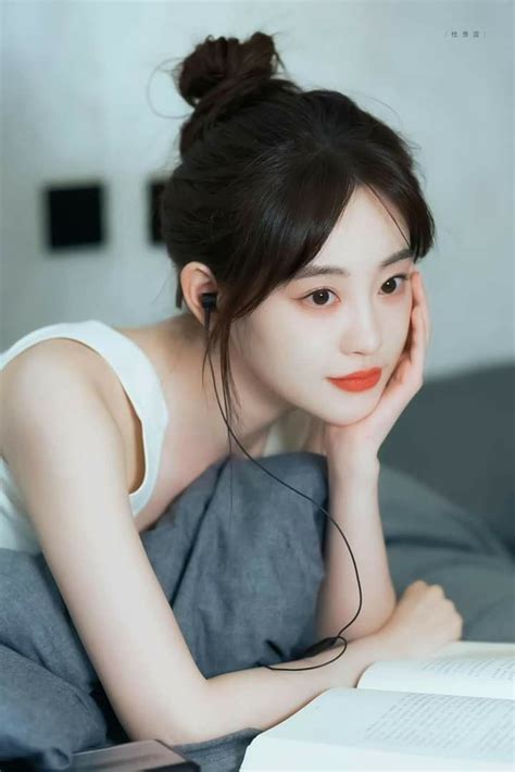 A Woman Laying On Top Of A Bed With An Open Book Next To Her Face