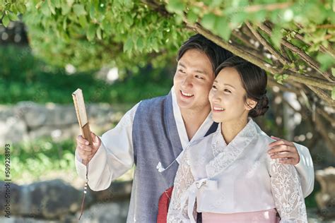 한국의 전통적인 한복을 입고 나무 그늘 밑에서 서있는 모습 젊고 아름답고 우아한 모습의 아시아 한국 남녀 모델 Stock