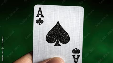 A Close Up Of An Ace Of Spades Playing Card Held Against A Green