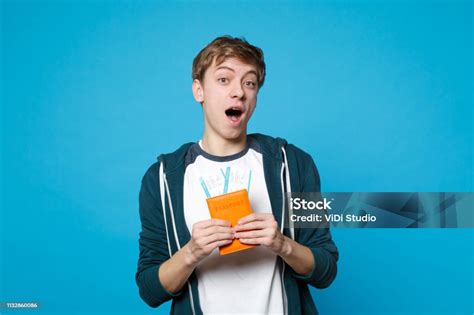 캐주얼에 입을 벌리고 여권 및 탑승권 표를 들고 파란색 벽 배경에 고립 된 우연한 옷을 입은 젊은 남자 충격 사람들은 진심으로 감정 라이프 스타일 개념입니다 복사 공간을