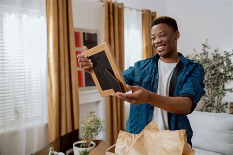 한 남자가 새 아파트로 이사한 후 거실에서 청소하고 골판지 상자를 풀고 소년은 어린 시절부터 프레임에 있는 사진을 발견하고 충격을 받고 기쁨으로 시계를 보냅니다 가구에 대한