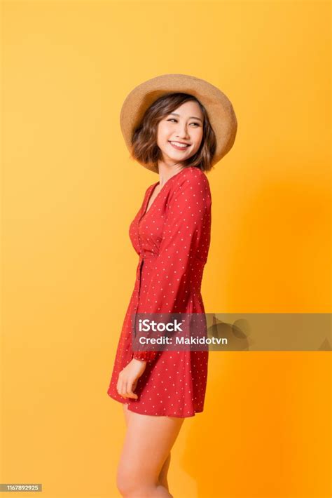 빨간 드레스와 밀짚 모자를 입고 오렌지 색 배경을 가진 행복한 활기찬 아시아 여성의 스튜디오 샷 갈색 머리에 대한 스톡 사진 및 기타 이미지 Istock