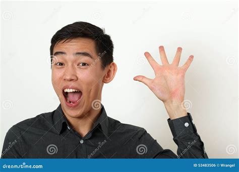 Smiling Young Asian Man Waving His Palm And Looking At Camera Stock