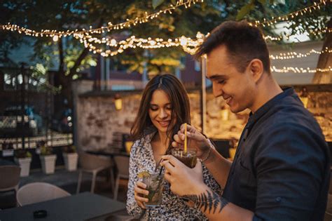 아름다운 커플남자와 여자는 쾌활한 분위기와 상쾌한 칵테일로 둘러싸인 오픈 테라스의 카페에서 여름 데이트를 즐깁니다 그들의 얼굴 표정은 함께 시간을 보내는 기쁨과 행복을