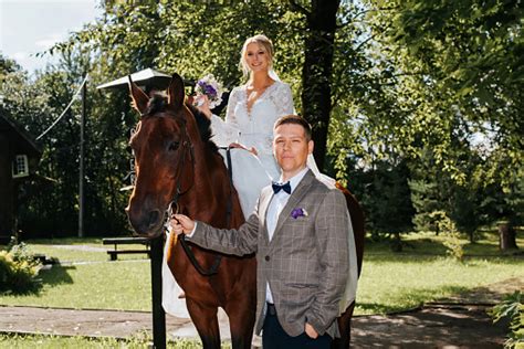 행복한 젊은 부부의 초상화 꽃다발이있는 흰색 드레스를 입은 신부는 양복을 입은 신랑이 근처에 서서 공원에서 야외에서 포즈를