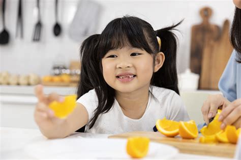 행복한 아시아 가족 오렌지 과일을 먹는 어린 소녀의 닫기와 어머니는 집에서 부엌에서 야채와 과일을 준비하고 있습니다 건강한 음식 개념 2명에 대한 스톡 사진 및 기타 이미지