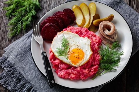 실험실 옥수수 쇠고기 튀긴 계란 얇게 썬 사탕무 절인 사탕무를 얹은 비트 뿌리가 있는 으깬 감자 나무 테이블에 있는 접시에 청어