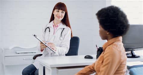흑인 아프리카 여성 환자는 젊은 자신감있는 유럽 의사와 병원에서의 건강에 대해 상담합니다 클립보드에 메모를 하는 의사 치료 건강 관리 및 보험 개념 사진
