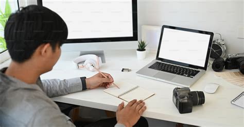 그래픽 디자이너 또는 사진 작가가 직장에서 여러 컴퓨터 앞에 앉아있는 동안 메모를하고 있습니다 사진 Unsplash의 태국 이미지