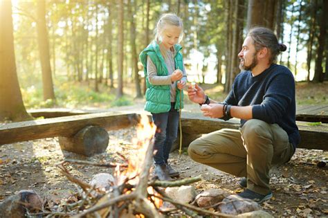 모닥불을 시작하는 법을 배우는 귀여운 어린 소녀 아버지는 딸에게 불을 피우라고 가르치시고 있습니다 캠프 화재에서 재미를 가진 아이 가을 숲에서 아이들과 캠핑 아버지에 대한