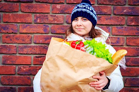 식품 슈퍼마켓 근처의 패키지와 함께 아름 다운 소녀 식료품가 게에서 쇼핑 하는 여자 따뜻한 옷과 모자 야채와 식료품 쇼핑 가방을 들고 있는 여자 가방에 대한 스톡 사진 및