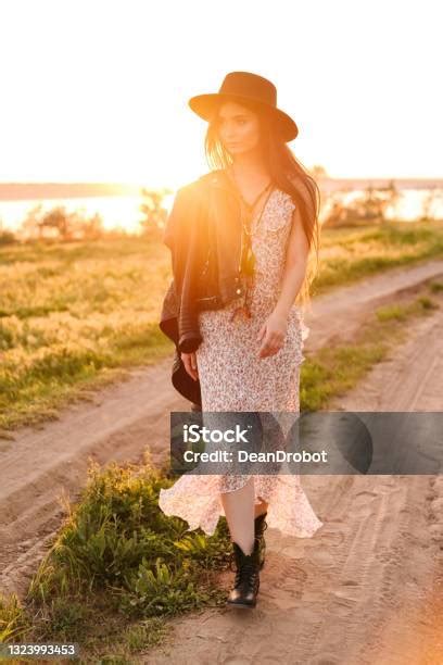 긴 머리를 입고 드레스와 모자를 쓰고 화창한 따뜻한 날에 시골에서 길을 걷는 세련된 백인 여성의 전체 길이 이미지 가죽에 대한