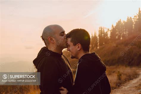 Side View Of Homosexual Couple Hugging And Kissing On Path In Forest In Sunny Day SuperStock