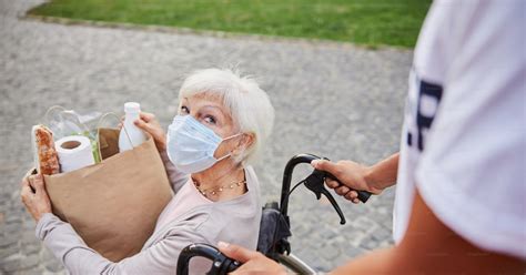 의료용 마스크를 쓰고 휠체어를 밀고 있는 누군가를 바라보며 구매한 종이 봉지에 구멍을 뚫고 있는 장애 노인 여성 사진 Unsplash의 코로나 바이러스 이미지