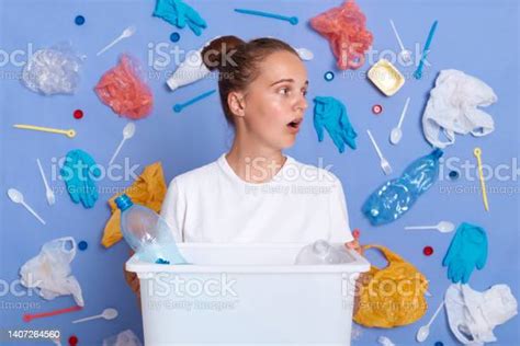 플라스틱 병이있는 충격을받은 여성 홀딩 박스의 실내 샷은 걱정스러운 표정을 가지고 있으며 입을 크게 벌린 플라스틱 쓰레기를 멀리 바라보고 큰 환경 문제의 심각성을 깨닫습니다